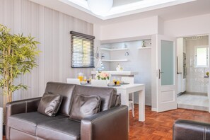 Uma sala de estar moderna com um sofá de couro, uma mesa de jantar com itens de café da manhã e uma cozinha visível por uma porta aberta.