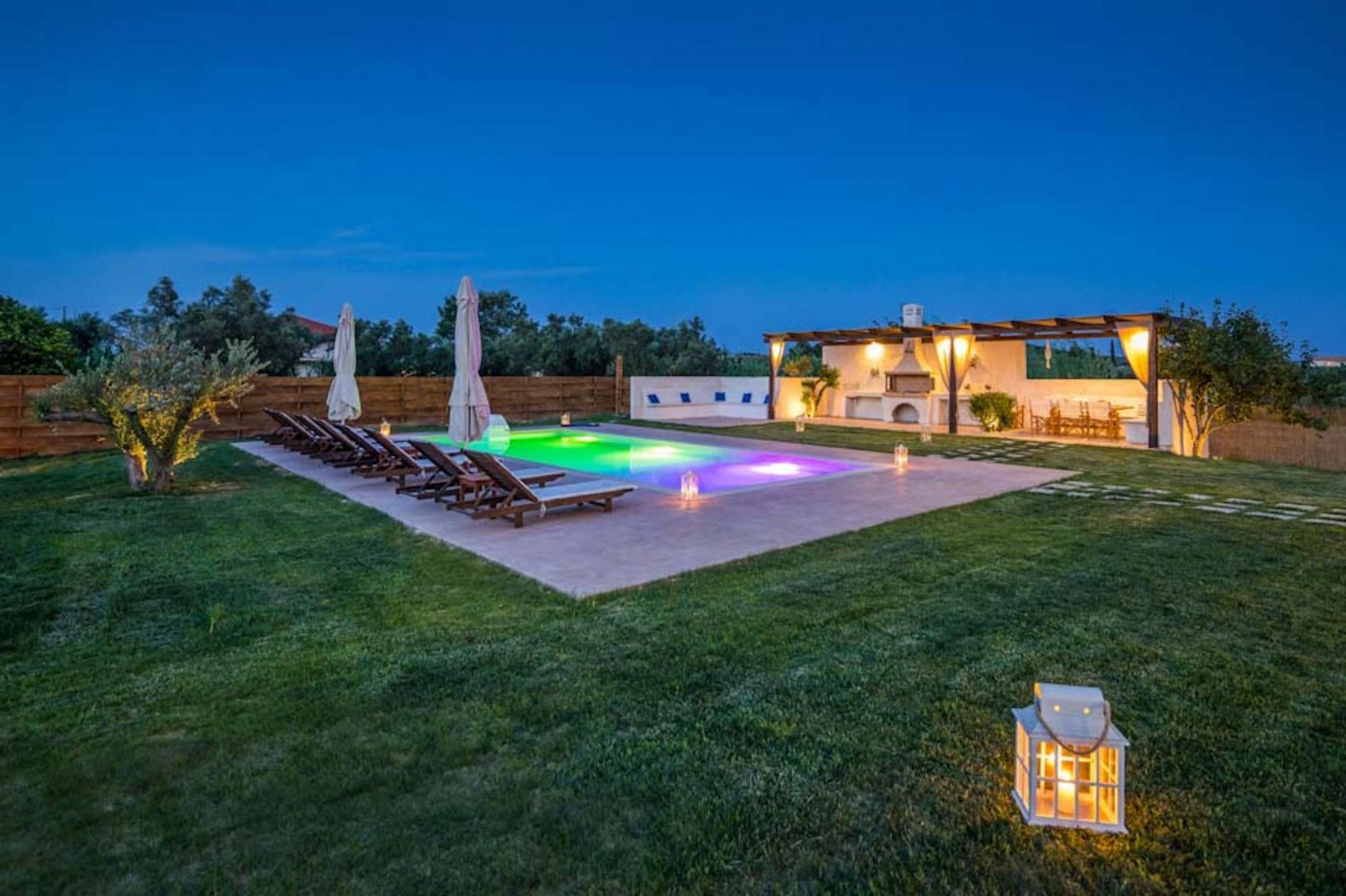 Um quintal bem cuidado com piscina, espreguiçadeiras e uma pérgula com iluminação.