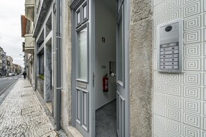 Uma rua estreita com edifícios de ambos os lados, um extintor de incêndio fixado na parede e um teclado na porta.
