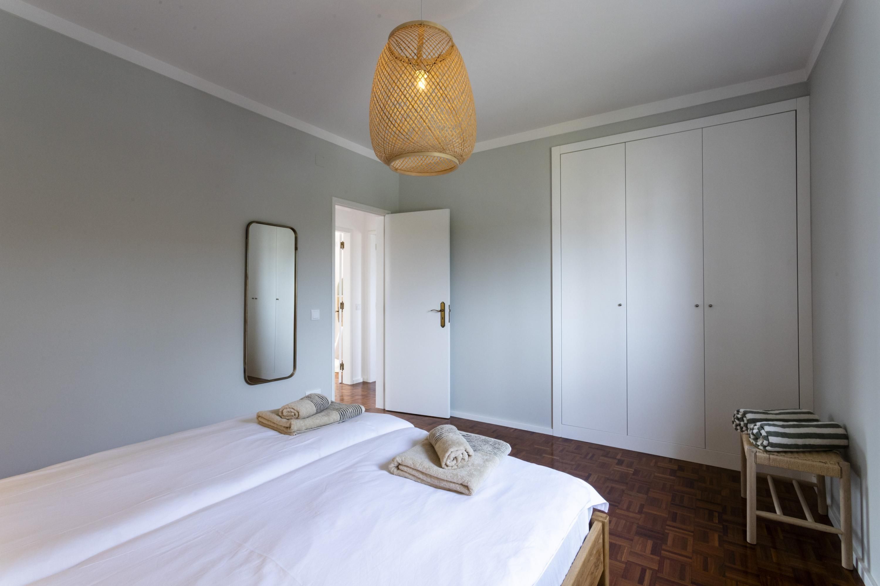 Quarto com cama grande, luminária pendente, espelho e guarda-roupa.