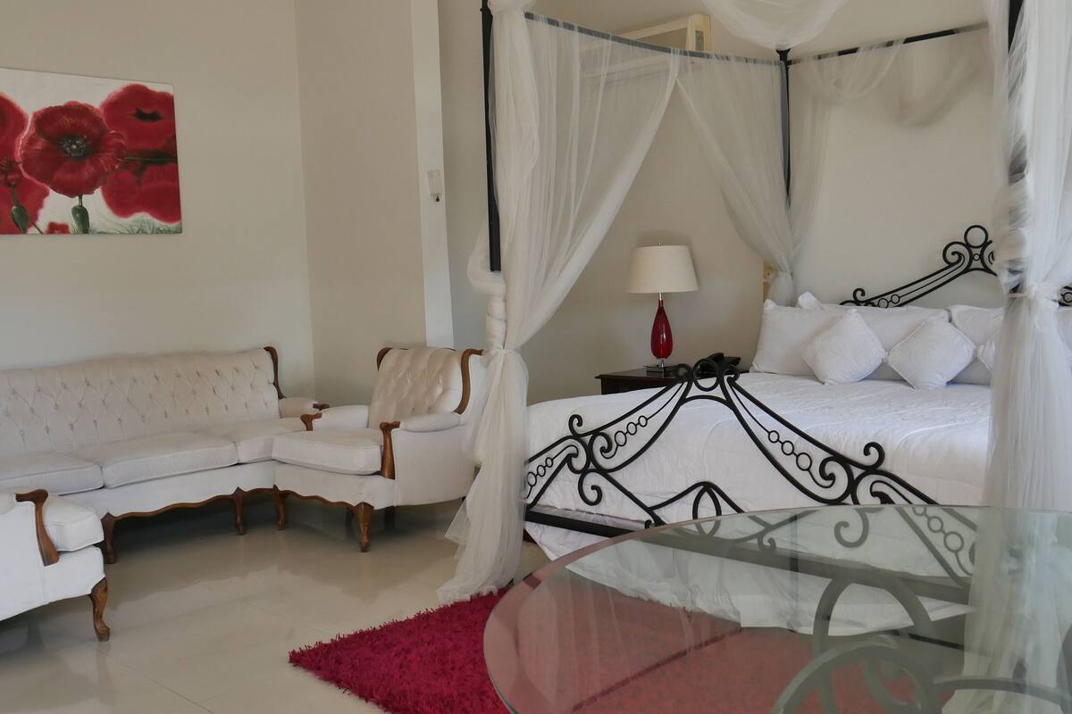 Quarto com uma cama de dossel, um sofá branco e uma mesa de centro de vidro.