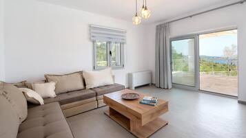 Uma sala de estar moderna com um sofá, uma mesa de centro e uma grande porta de vidro deslizante que dá para uma área externa.