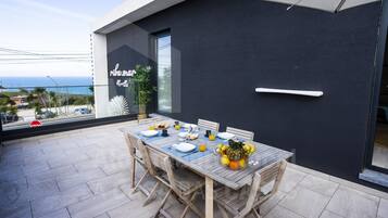 Uma área de refeições com uma mesa posta para quatro pessoas, uma parede preta com uma janela e vista para o mar.