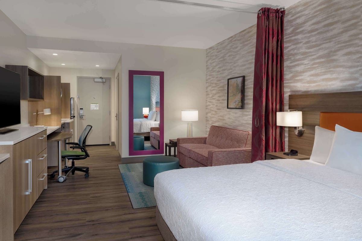 Quarto de hotel com cama, escrivaninha, cadeira e espelho.