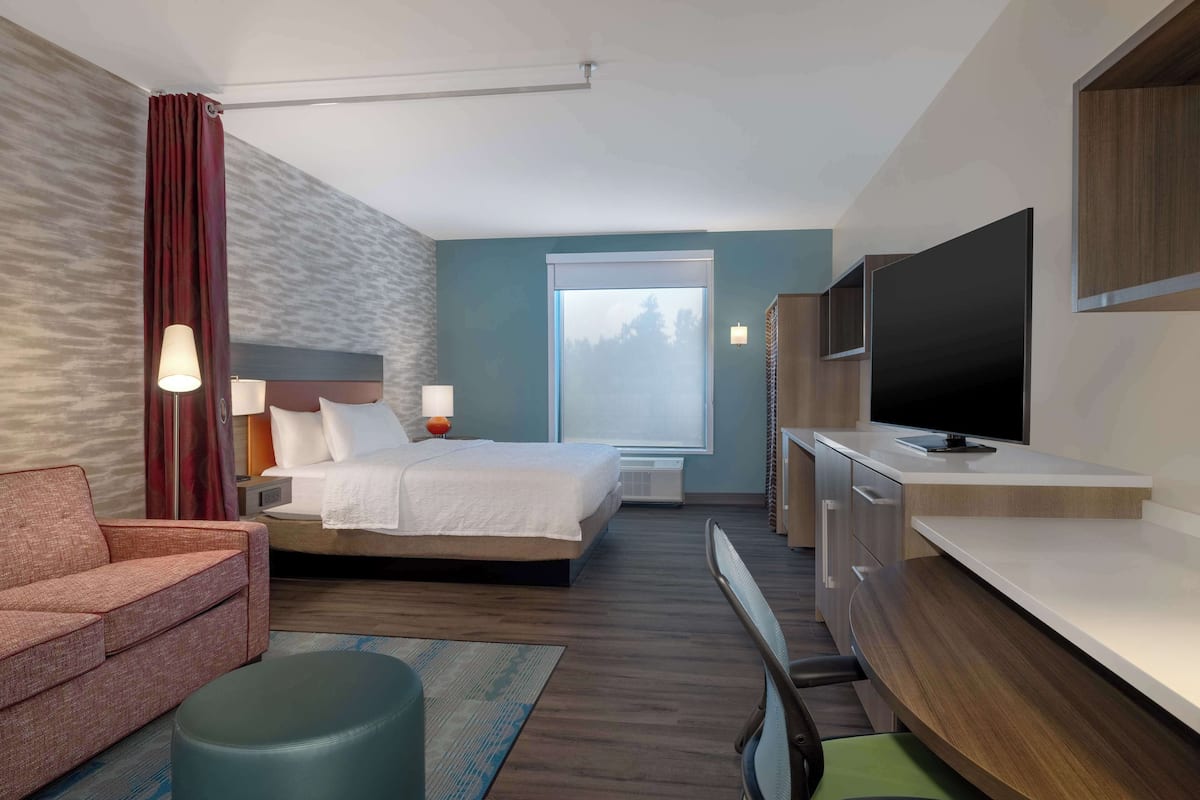 Quarto de hotel com cama, escrivaninha, televisão, sofá e janela.