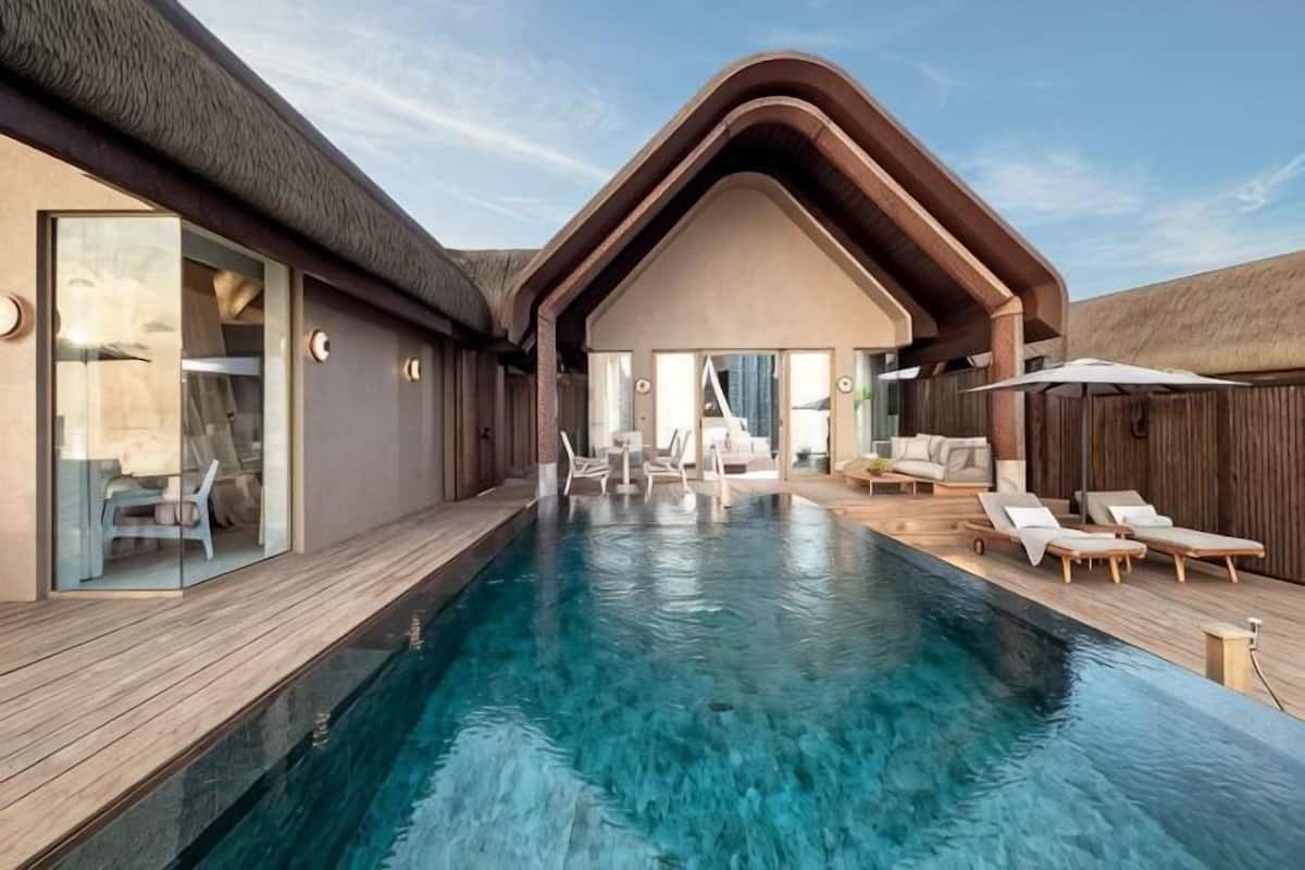 Piscina com espreguiçadeiras, área de estar coberta e um edifício com grandes janelas.