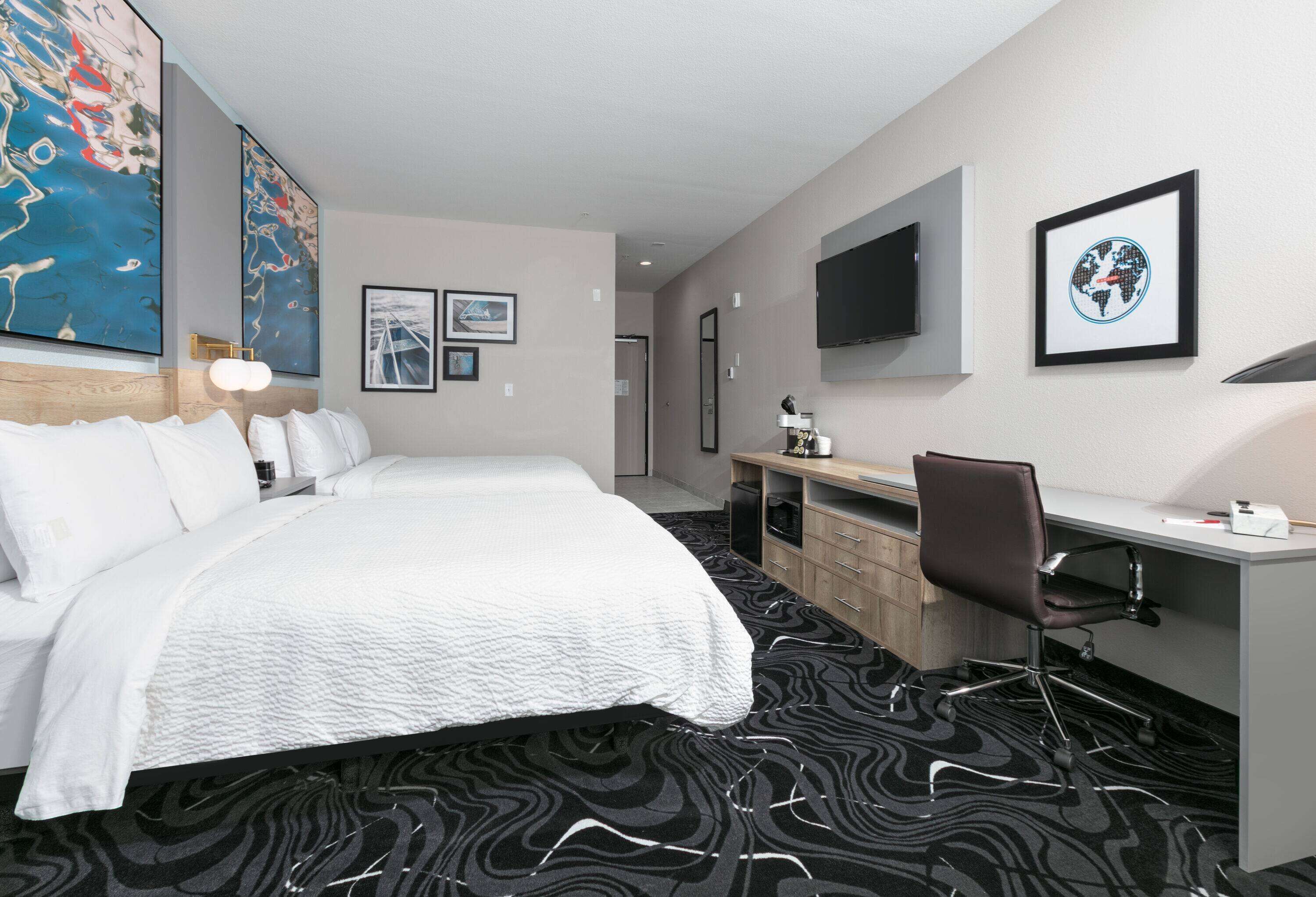 Quarto de hotel com uma cama grande, uma escrivaninha, uma cadeira e obras de arte nas paredes.