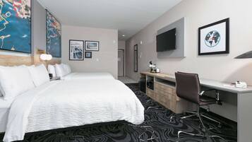 Quarto de hotel com uma cama grande, uma escrivaninha, uma cadeira e obras de arte nas paredes.