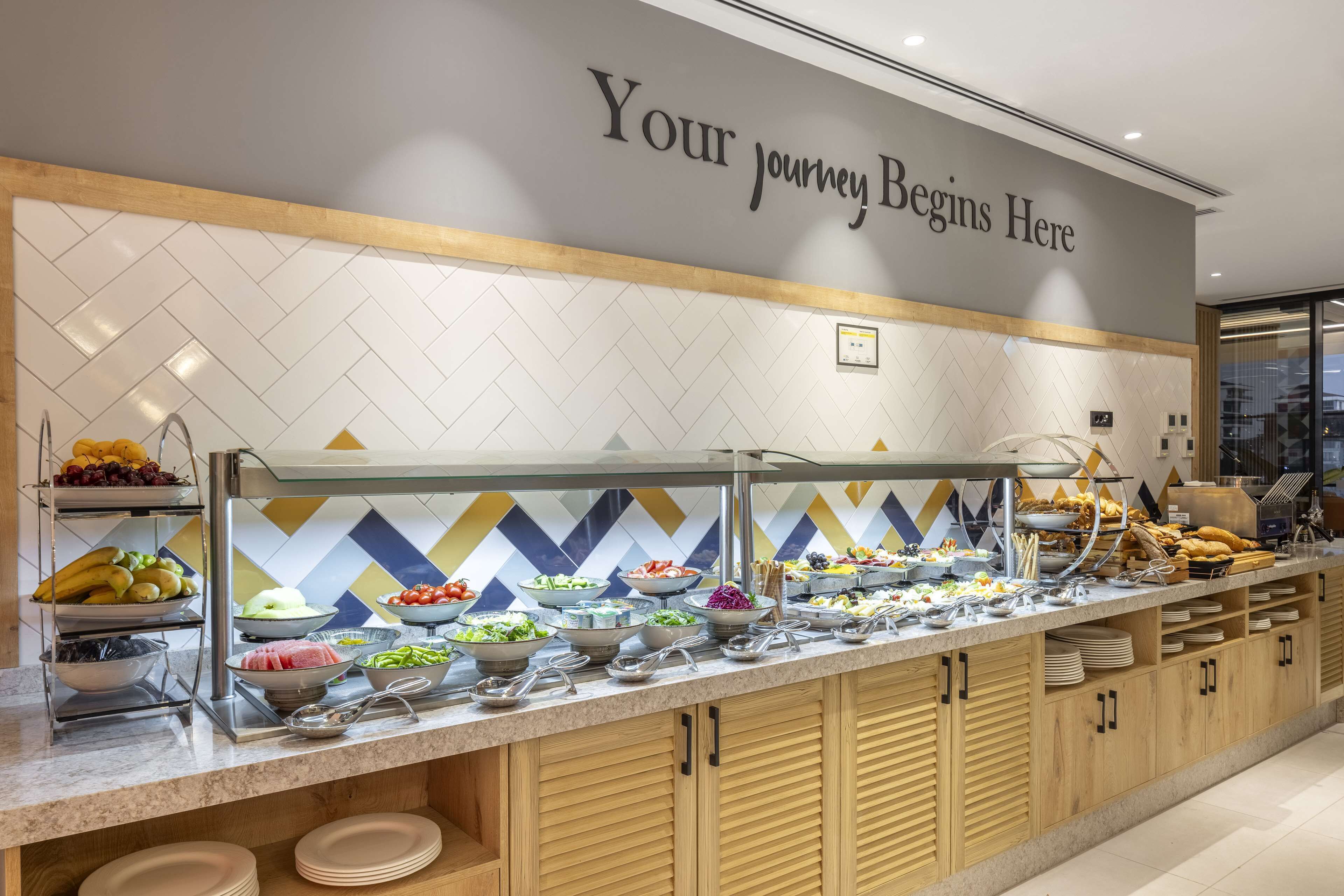 Buffet com diversos alimentos e um letreiro com a mensagem 'A sua jornada começa aqui'.