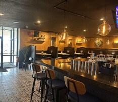 Interior de restaurante com bancada de bar, iluminação pendente e prateleiras decorativas na parede.
