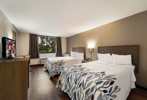 Quarto de hotel com duas camas, uma escrivaninha, televisão e janela com cortinas.
