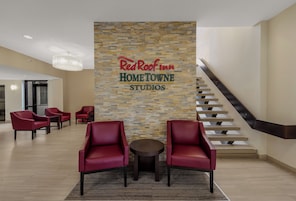Lobby do Red Roof Inn Hometown Studios com parede de pedra, poltronas de couro vermelho, uma pequena mesa e uma escada.