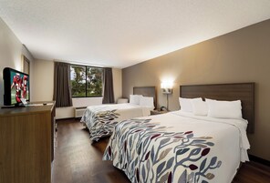 Quarto de hotel com duas camas, uma escrivaninha, televisão e janela com cortinas.