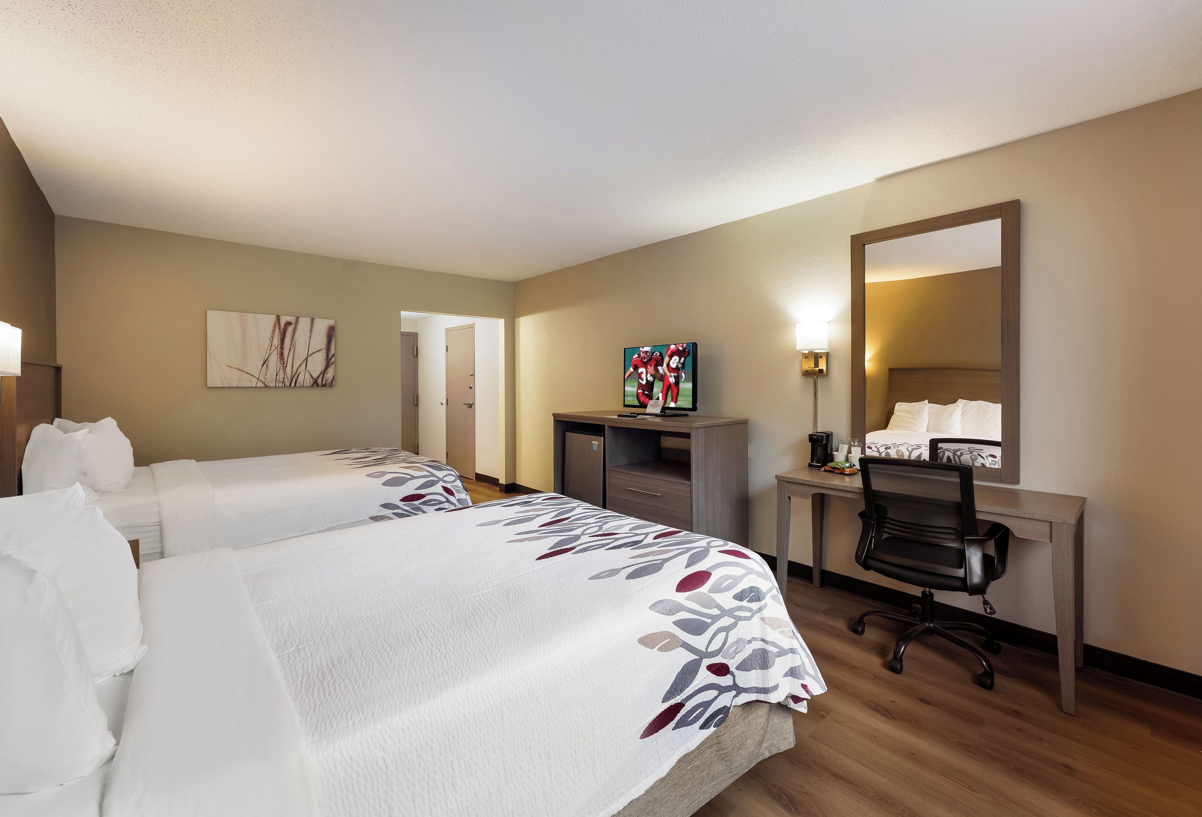 Quarto de hotel com duas camas, uma escrivaninha, uma cadeira, uma televisão e um espelho.