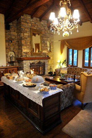 Uma sala de estar acolhedora com lareira de pedra, um candelabro e um espaço de jantar com uma mesa coberta por um tecido rendado.