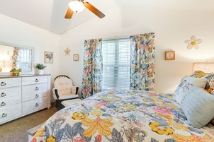 Quarto com colcha florida, cômoda, cadeira e ventilador de teto.