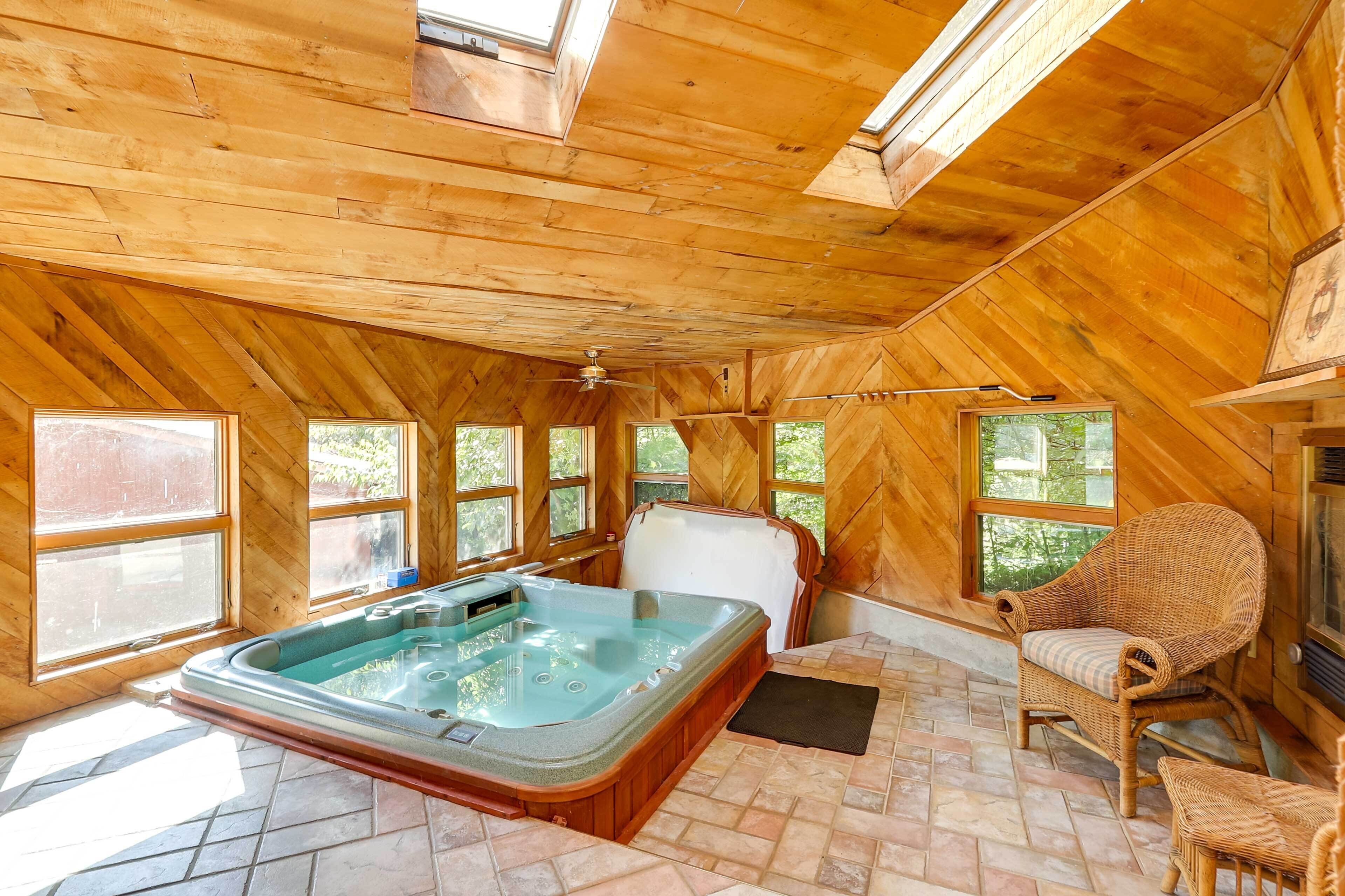Uma cabana de madeira com hidromassagem, móveis de vime e janelas amplas.