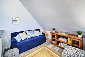 Uma sala de estar aconchegante com um sofá azul, almofadas estampadas, uma mesa lateral de madeira com livros e um tapete tecido.