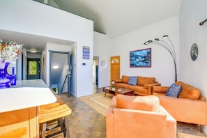 Uma sala de estar moderna com sofá, mesa de centro e área de jantar com mesa de madeira e banquetas.