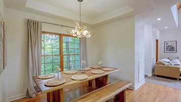 Uma sala de jantar com uma longa mesa de madeira, jogos americanos trançados e um candelabro.