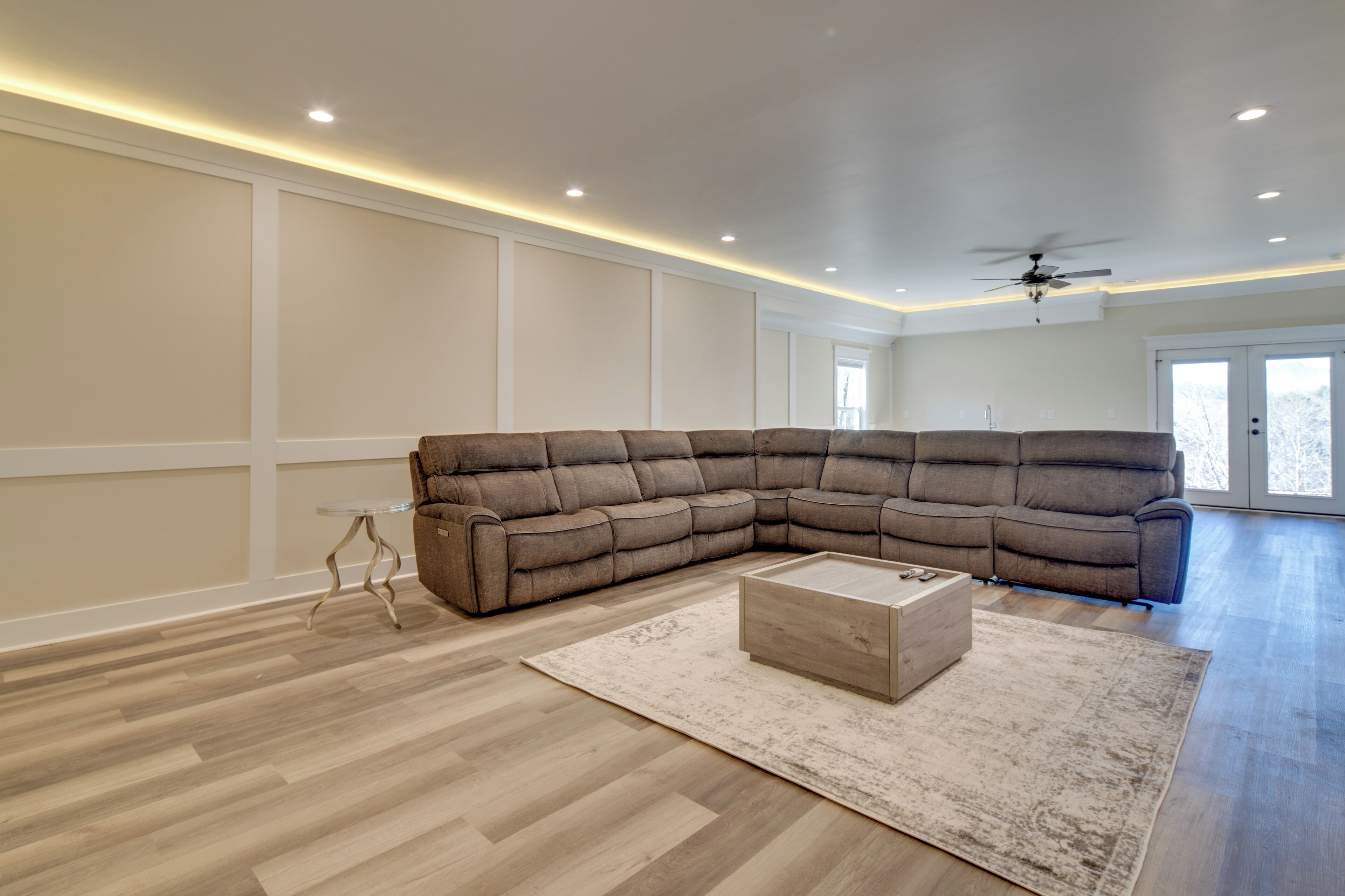 Uma sala de estar ampla com um sofá seccional em formato de L, uma mesinha lateral e uma mesa de centro de madeira.