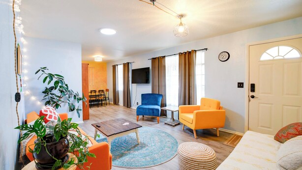 Uma sala de estar moderna com sofá, poltronas, mesa de centro e uma área de jantar ao fundo.
