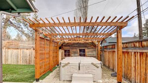 Uma área de estar coberta ao ar livre, com pérgola, degraus de pedra e cerca de madeira.