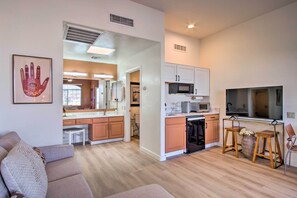 Uma sala moderna com sofá, área de jantar com televisão e cozinha com armários e micro-ondas.