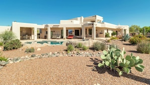 Uma casa moderna de dois andares com piscina, rodeada por paisagismo desértico com cactos e plantas de agave.