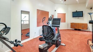 Uma academia em casa com equipamentos de cardio, televisão e ventilador de teto.
