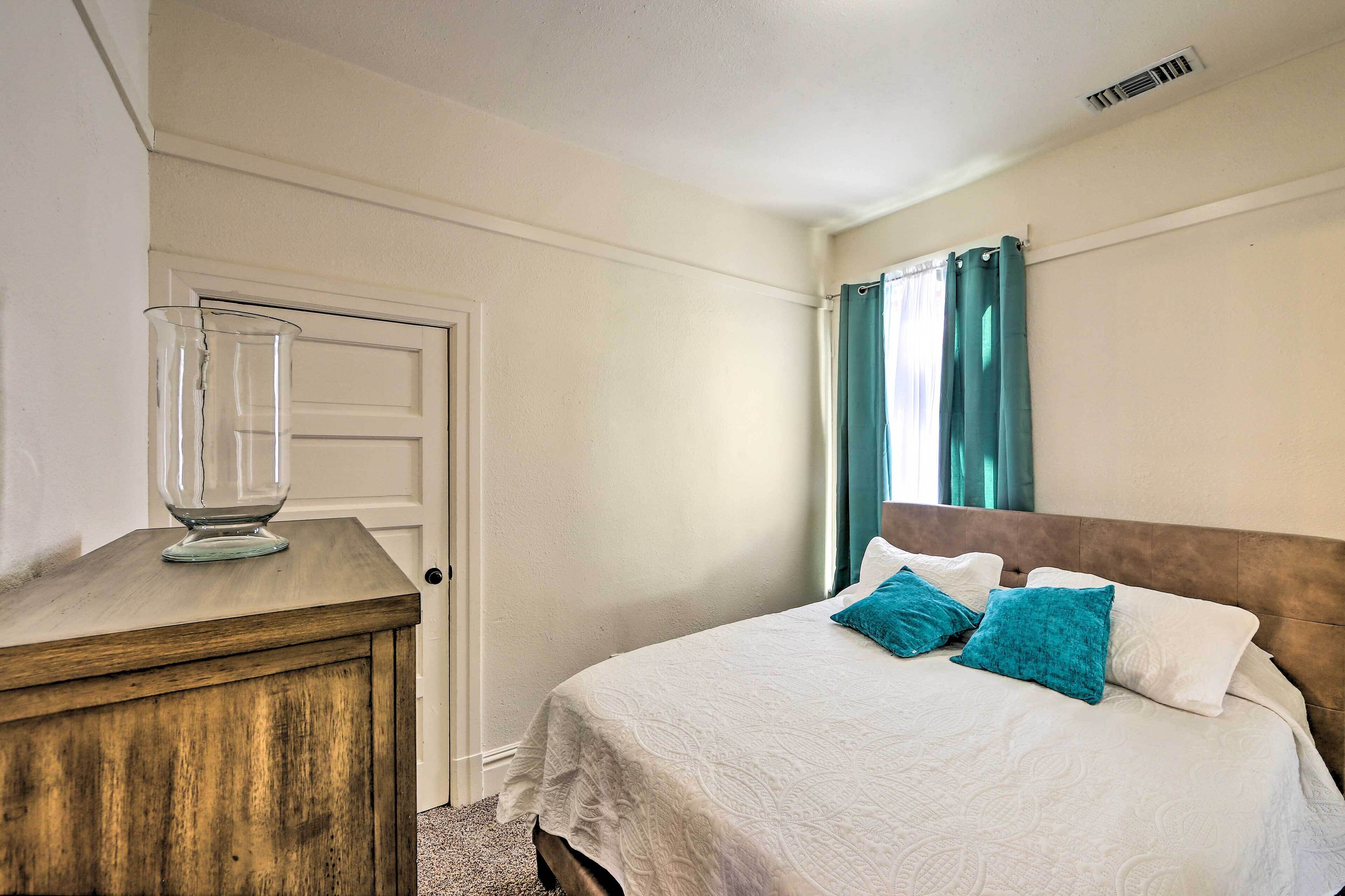Quarto com cama, mesa de cabeceira de madeira e uma porta.