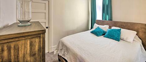 Quarto com cama, mesa de cabeceira de madeira e uma porta.