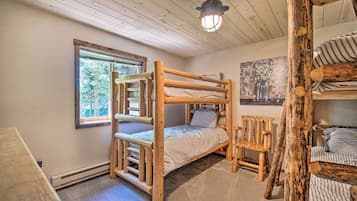 Quarto de cabana rústica com beliche, uma cadeira de madeira, janela com vista para árvores e ventilador de teto.
