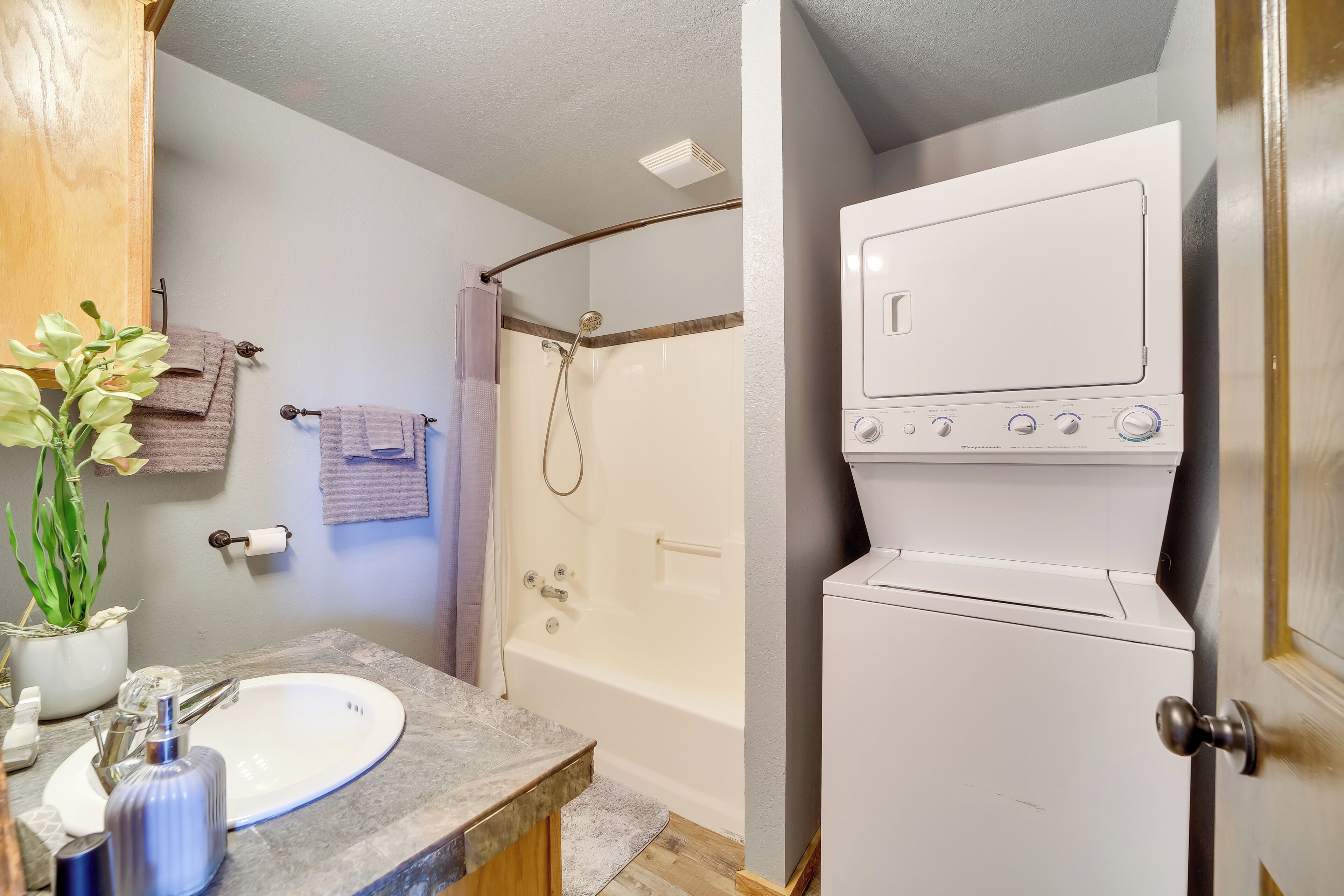 Casa de banho com lavatório, chuveiro e eletrodoméstico branco, possivelmente uma máquina de lavar ou secadora.