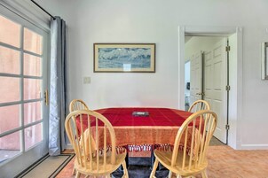 Uma sala de jantar com uma mesa posta para quatro pessoas, um quadro emoldurado na parede e uma porta que dá para outro cômodo.
