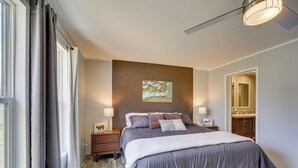 Quarto com cama grande, mesas de cabeceira, cabeceira, quadro e banheiro visível através de uma porta aberta.
