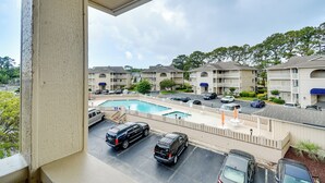 Vista de um hotel com piscina, várias vagas de estacionamento e uma galeria coberta.