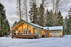 Uma cabana de toras com uma varanda grande e uma garagem, rodeada por uma paisagem coberta de neve e árvores altas.