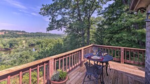 Um deck de madeira com mesa e cadeiras, com vista para um vale arborizado.
