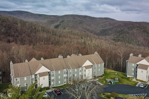 Um conjunto habitacional com vários apartamentos, rodeado por uma paisagem arborizada e montanhosa.