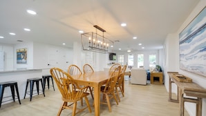 Uma cozinha moderna com uma mesa de jantar e cadeiras de madeira, um lustre pendurado e vista para a sala de estar.