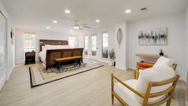 Quarto moderno com uma cama grande, mesa de cabeceira, abajur, ventilador de teto e vista para o exterior pelas janelas.