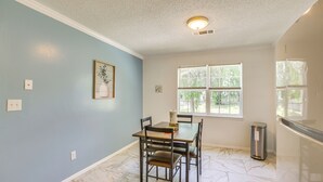 Uma área de refeições com mesa e cadeiras, uma janela com persianas e uma lixeira.