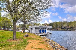 Uma cabana à beira do lago, com um cais, rodeada por árvores e uma área gramada.