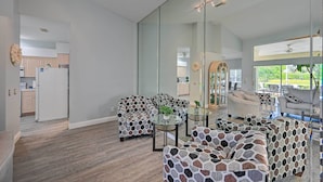 Sala de estar moderna com divisória de vidro, cozinha ao fundo e vista para o exterior.