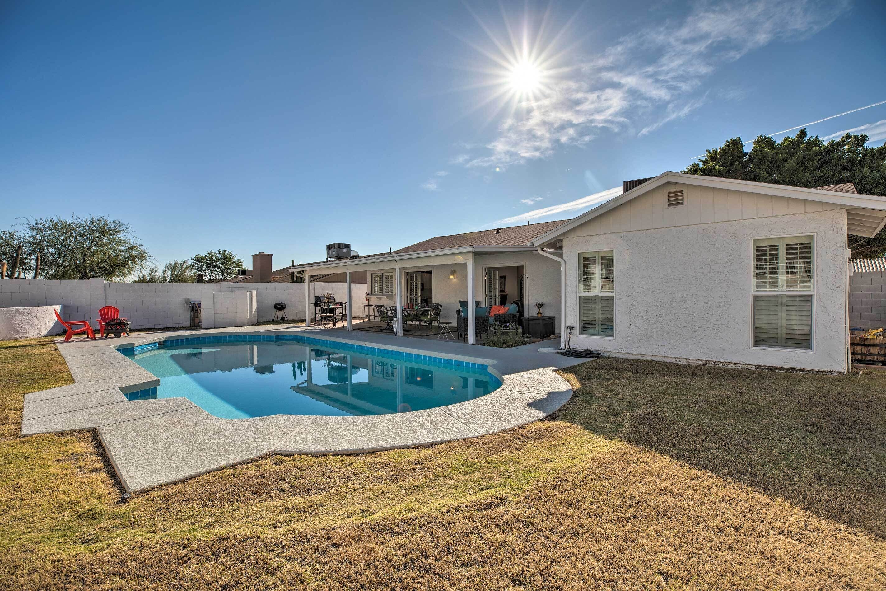 Um quintal com piscina, varanda coberta e casa com fachada branca.