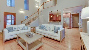 Uma sala de estar ampla com um conjunto de sofá branco, uma mesa de centro de madeira e uma escada que leva a um andar superior.