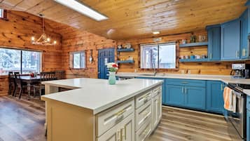 Uma cozinha no estilo cabana, com paredes de madeira, uma ilha central, armários azuis e uma área de jantar com mesa e cadeiras.