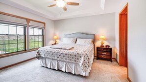Quarto com cama, duas mesas de cabeceira com abajures, ventilador de teto e janela com vista para o exterior.