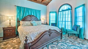 Quarto com uma cama grande, duas mesas de cabeceira, uma cadeira e uma janela com cortinas.